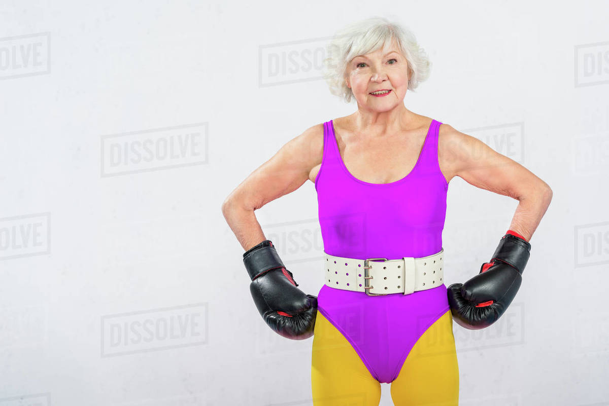 Happy senior sportswoman in boxing gloves standing with hands on waist ...