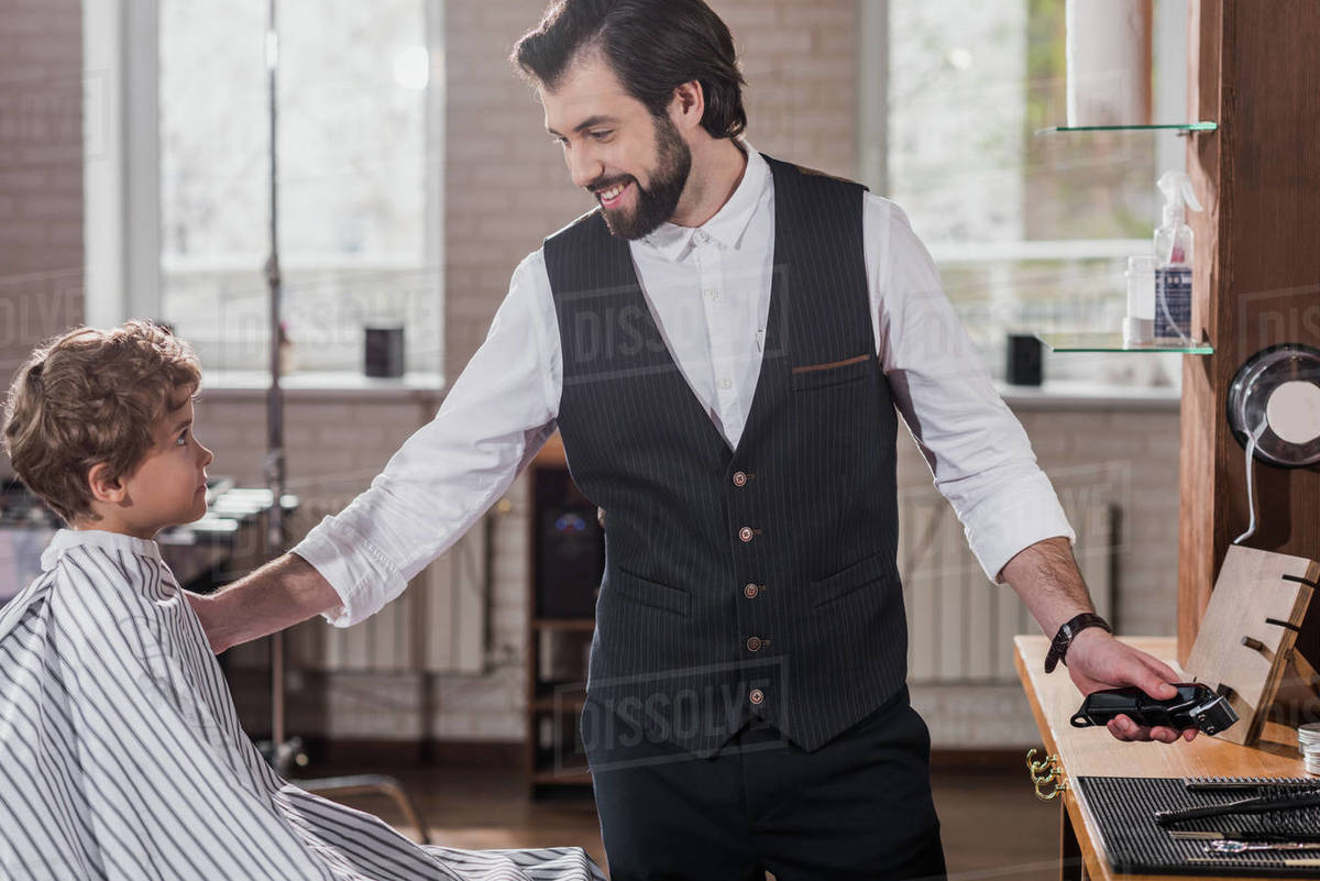 Smiling barber with Hair Clipper preparing to cut hair of adorable ...