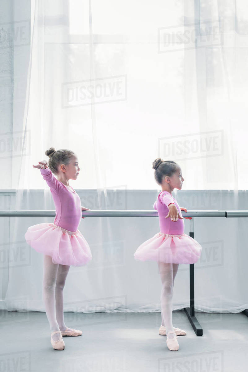 Side view of cute small ballet dancers exercising in ballet school ...
