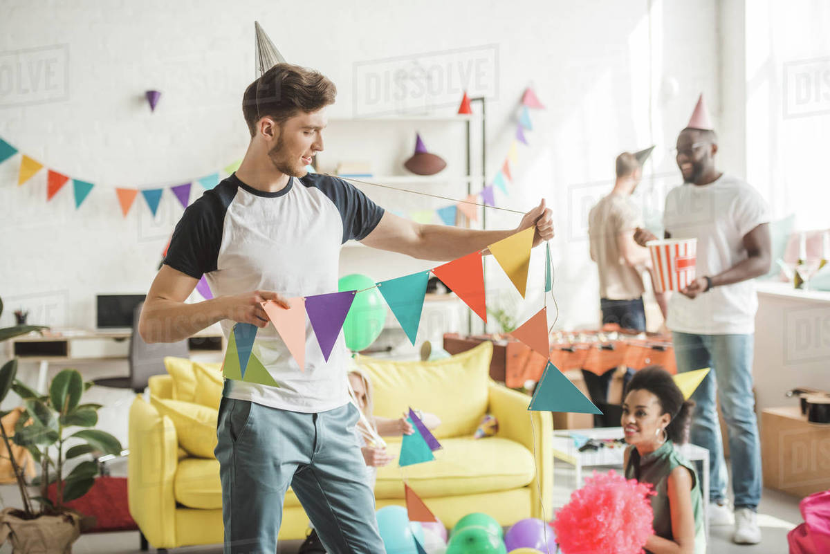Young man in party hat holding string with party garlands and friends ...