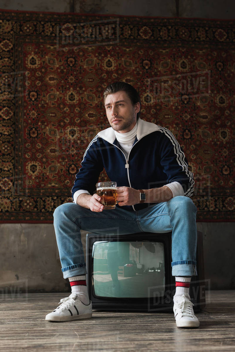 Stylish young man in vintage clothes with mug of beer sitting on retro ...