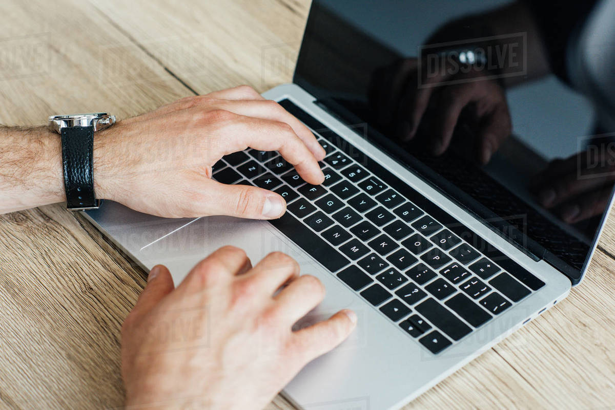 close-up partial view of person typing on laptop with blank screen ...