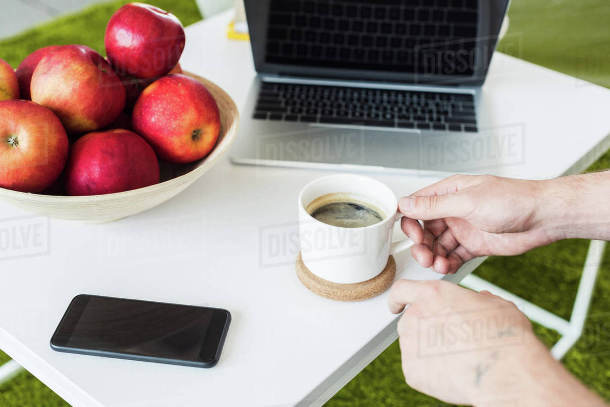 Cropped image of man taking coffee cup from table with smartphone ...