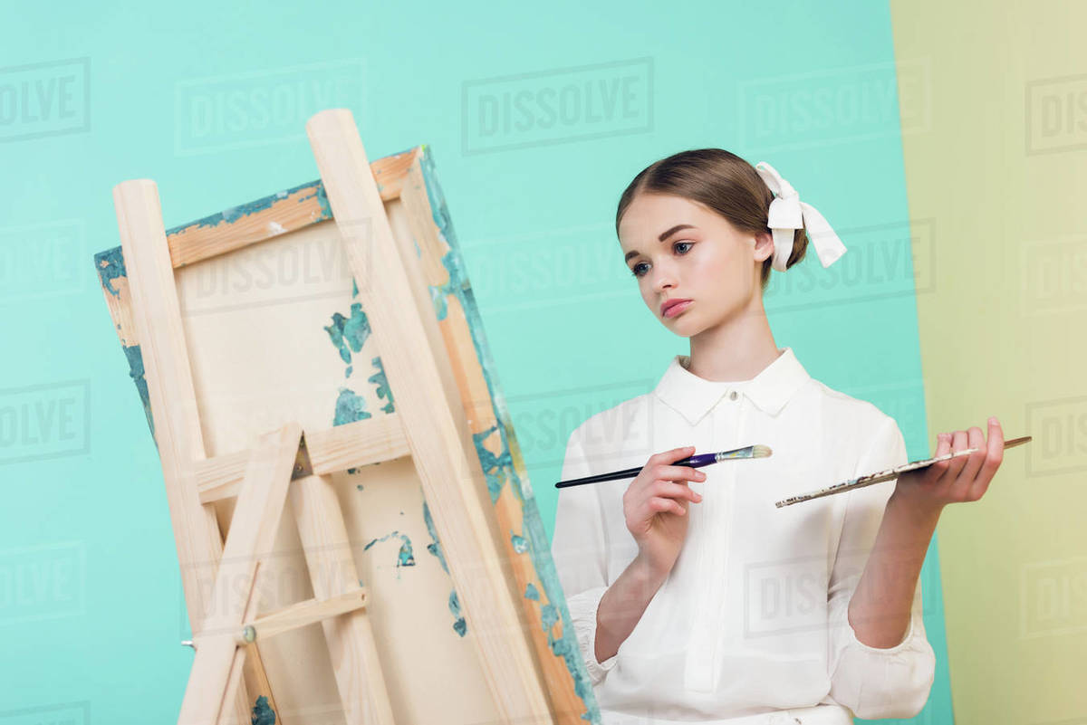beautiful teen artist painting on easel with brush and palette, on ...