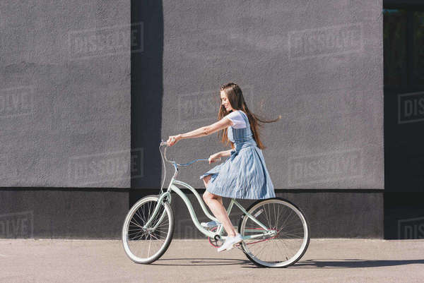 side view of young happy woman riding on bicycle - Stock Photo - Dissolve