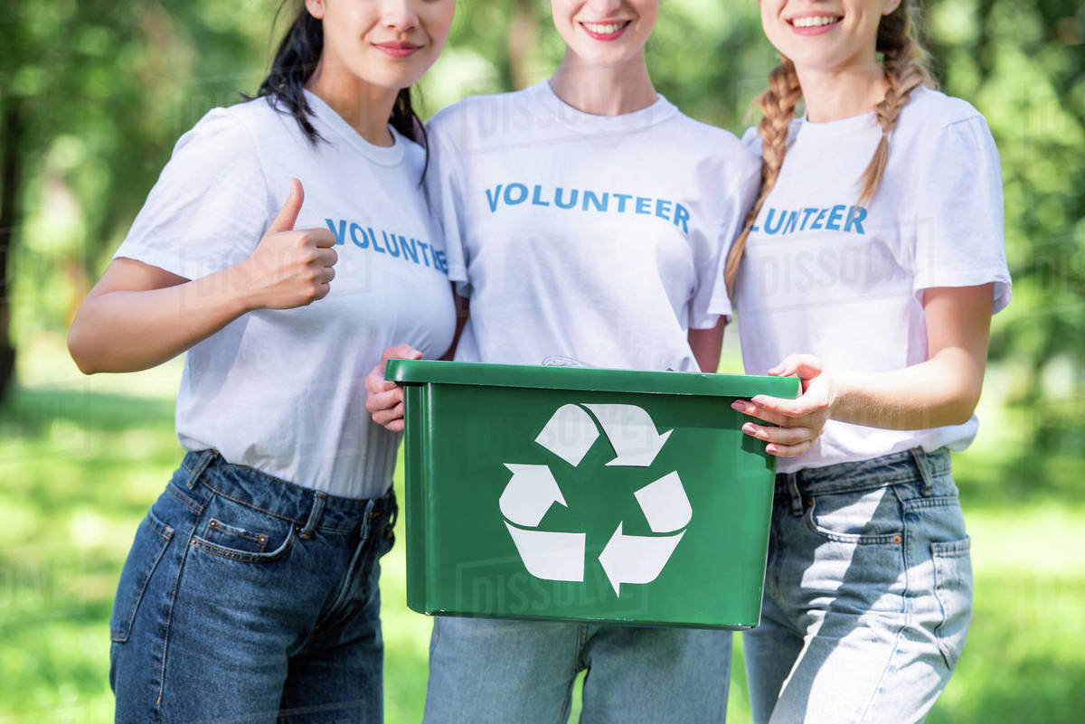 Cropped view of young volunteers with green recycling box showing thumb ...