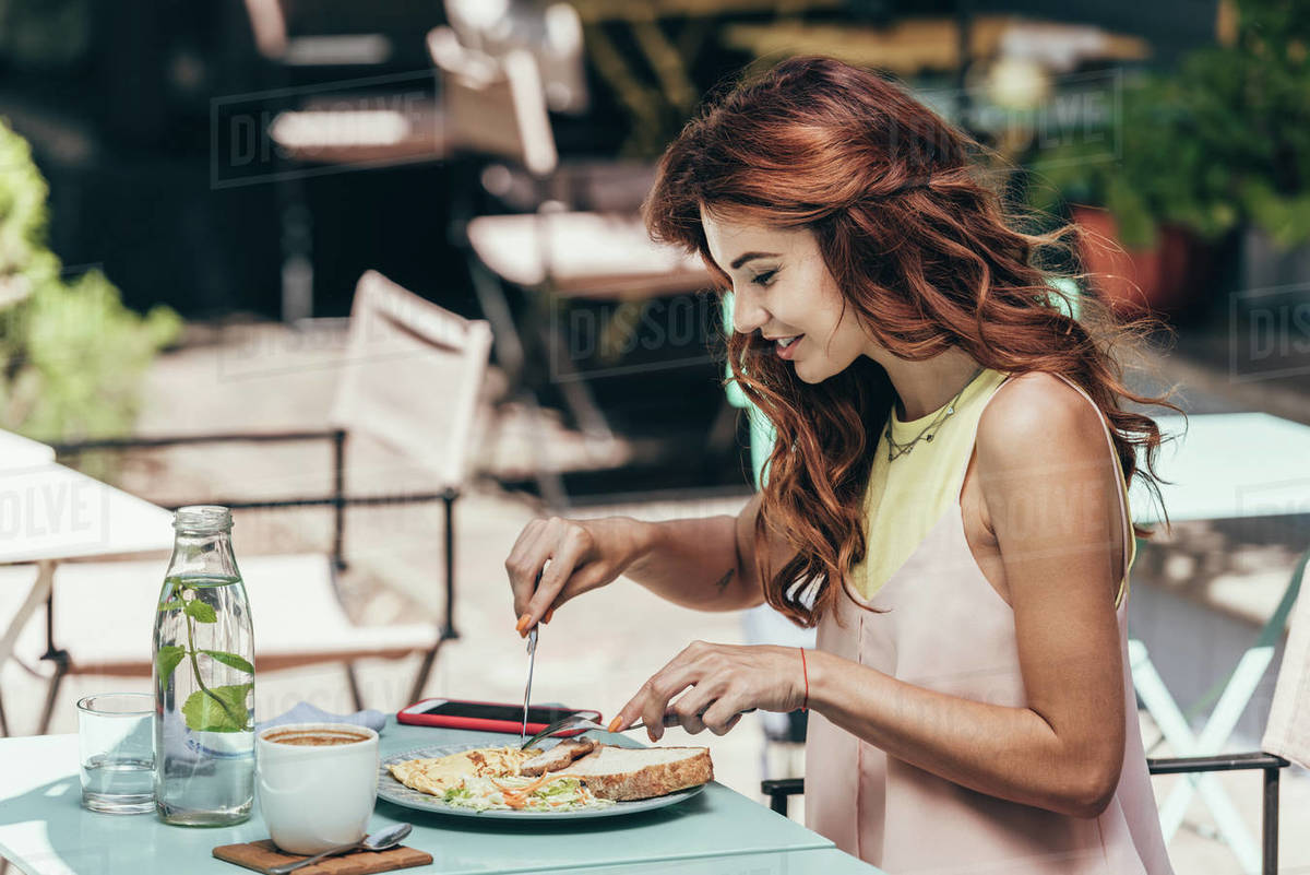 Side view of young woman having lunch alone in restaurant - Royalty ...