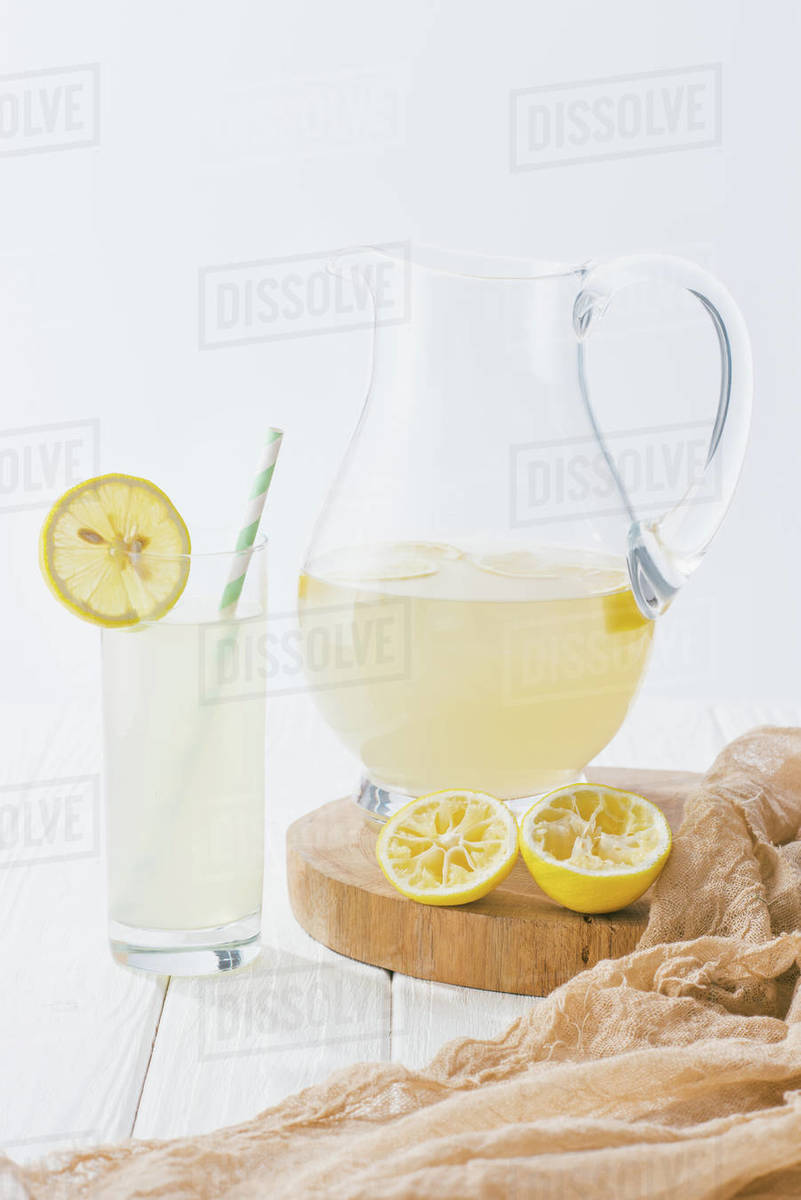 Close up view of lemonade in glass with straw and jug on white wooden ...