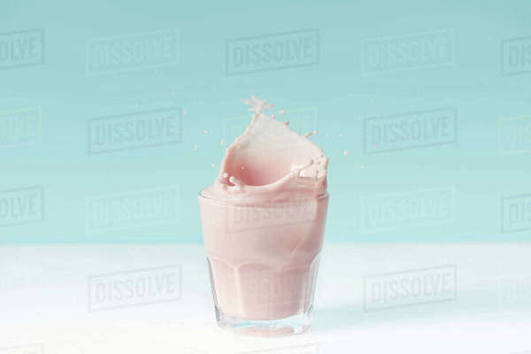 Splashing drops of strawberry milkshake from glass on blue background ...