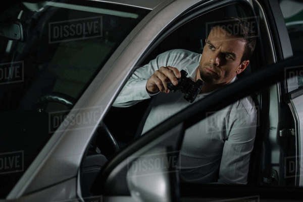 Focused undercover male agent doing surveillance by binoculars from his ...