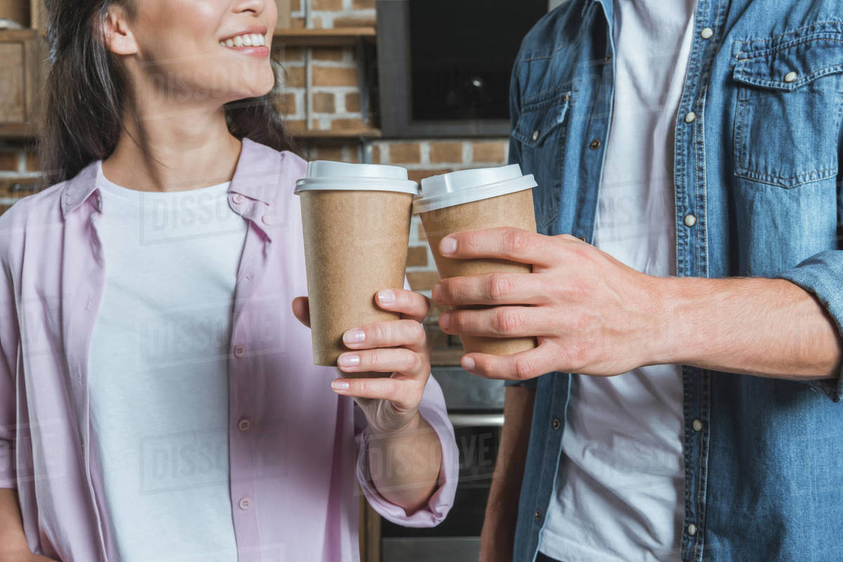 Cropped shot of couple clinking paper cups of coffee at kitchen ...