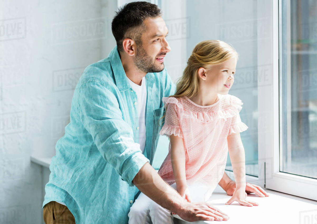 Happy father and cute little daughter looking at window together at ...