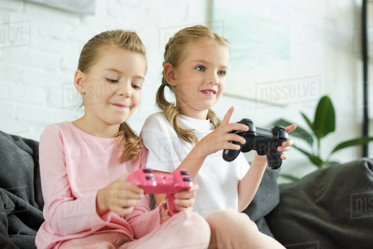 Portrait of little sisters with gamepads playing video game together at ...