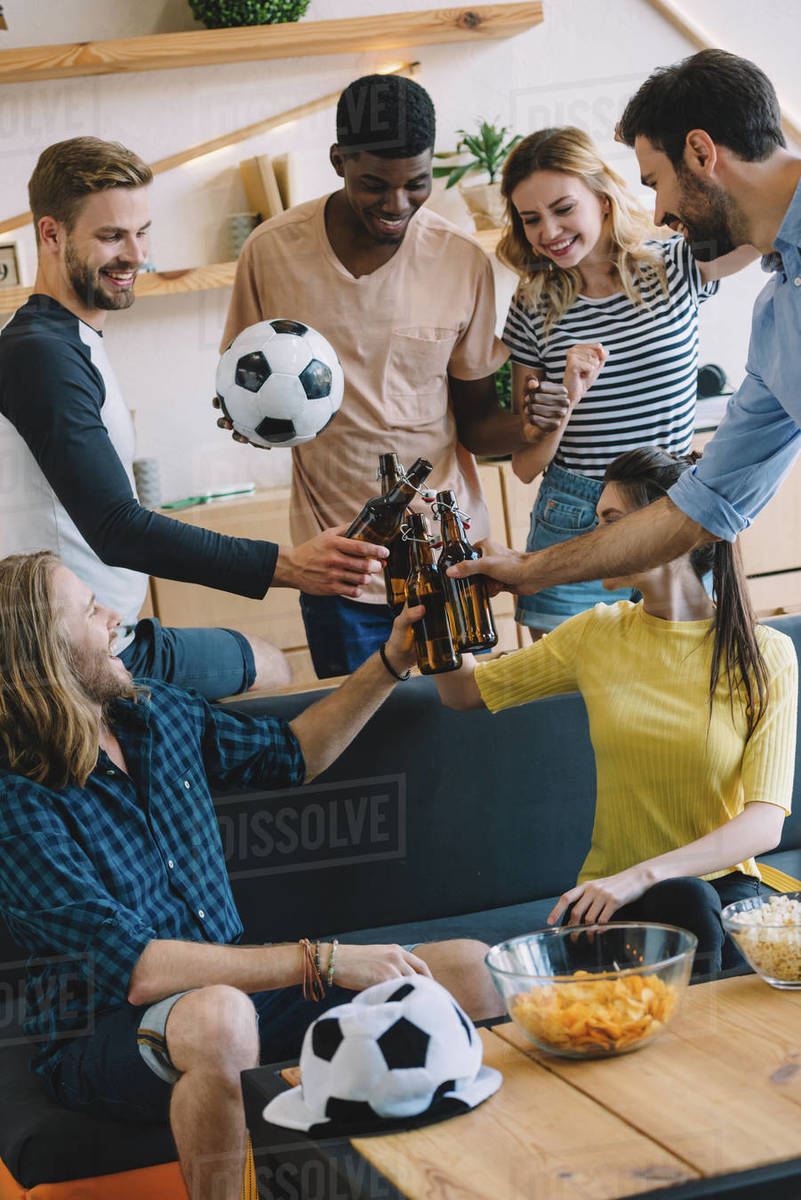 Group of multicultural friends with soccer ball clinking by beer ...