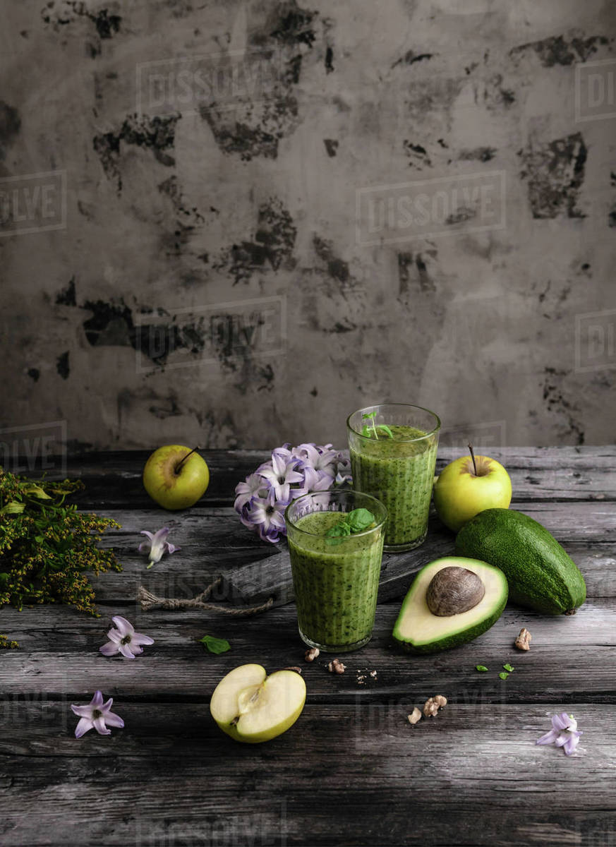 Green fruit smoothie in glasses on wooden background with flowers ...