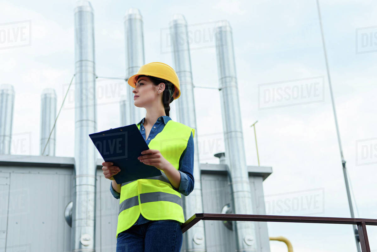 beautiful female builder in safety vest and hardhat writing in ...