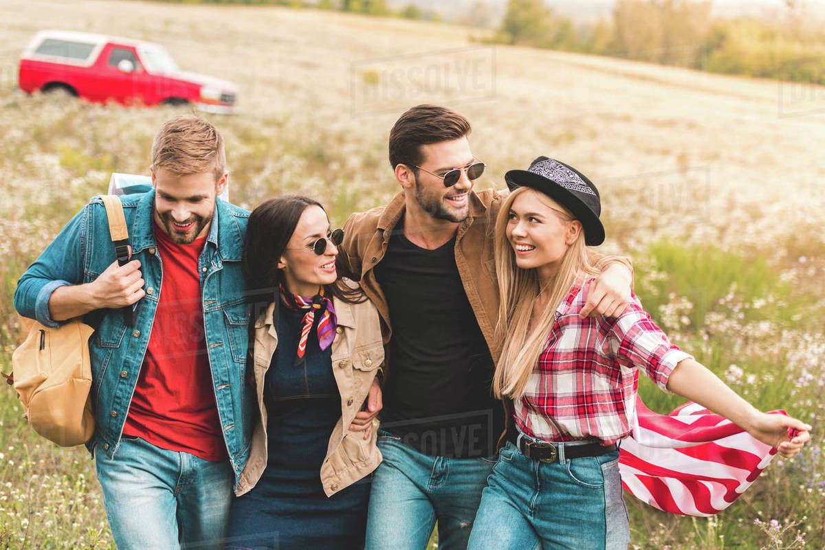 group of young friends embracing and walking by field together during ...