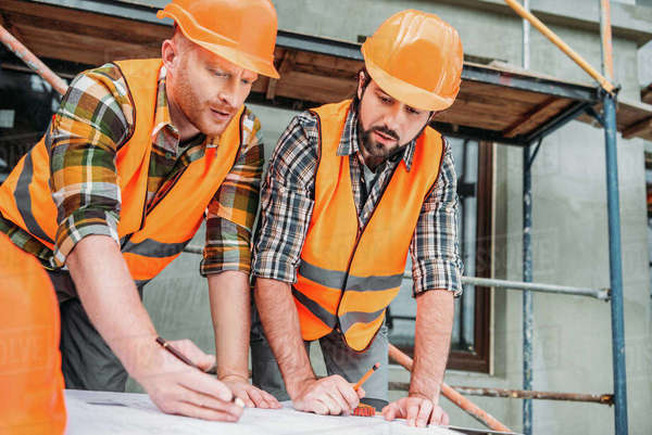 Confident builders drawing building plan at construction site - Royalty ...