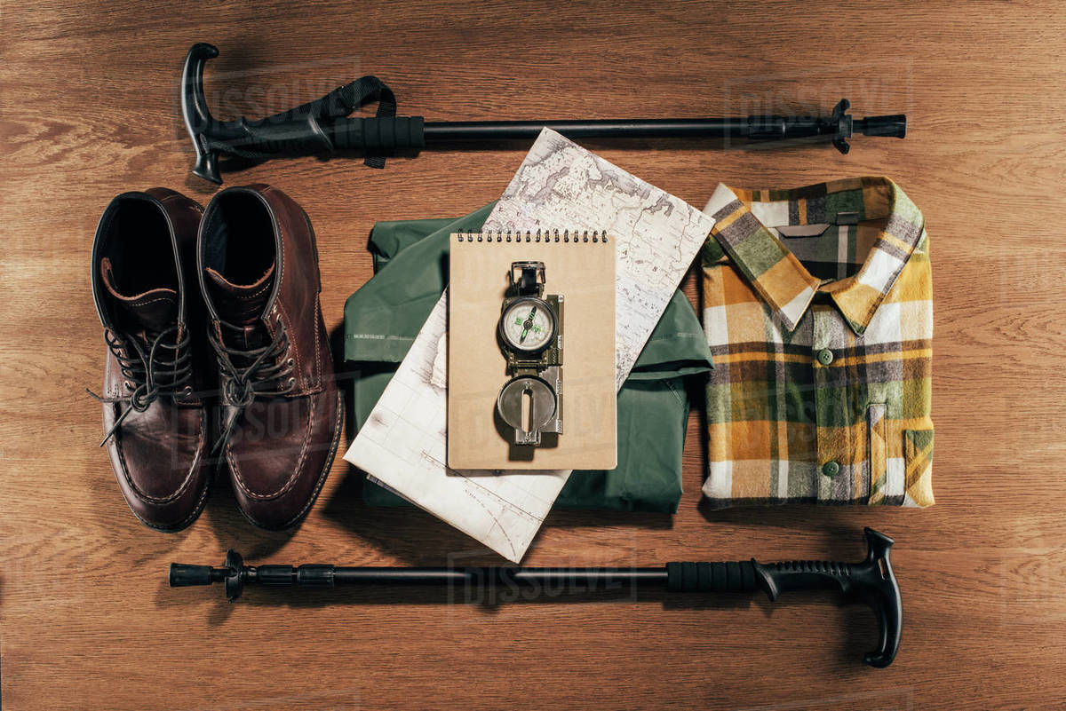 flat lay with trekking sticks, compass, map and clothes with footwear ...