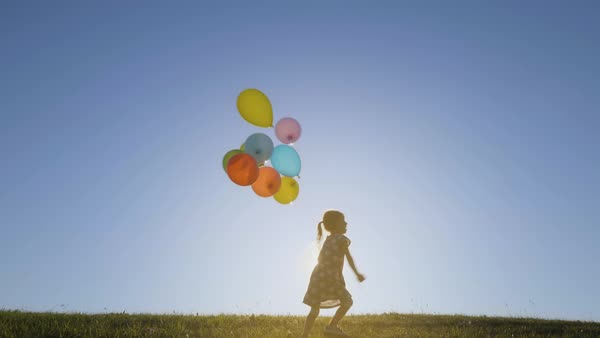 Little girl spinning and falling while holding up some balloons, filmed ...
