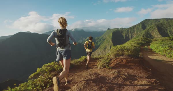 Active young couple running together on a mountain top ridge with lush ...