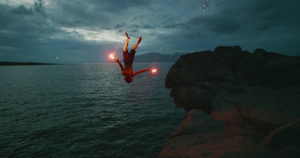 Extreme cliff jumping man backflipping off of an sea cliff with burning ...