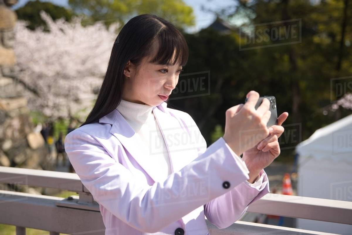 A portrait of Japanese woman shooting by smartphone behind cherry ...