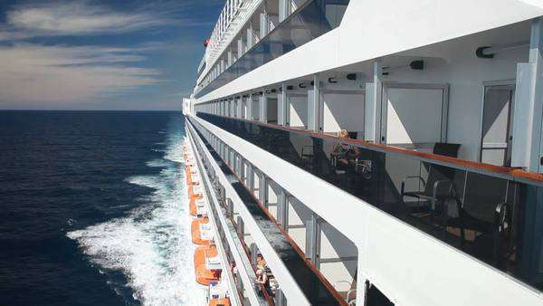 Cruise ship with passengers on balconies, lifeboats, and ocean wake ...