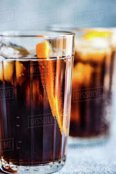 Close-Up of two cola drinks with ice cubes and a slice of orange ...