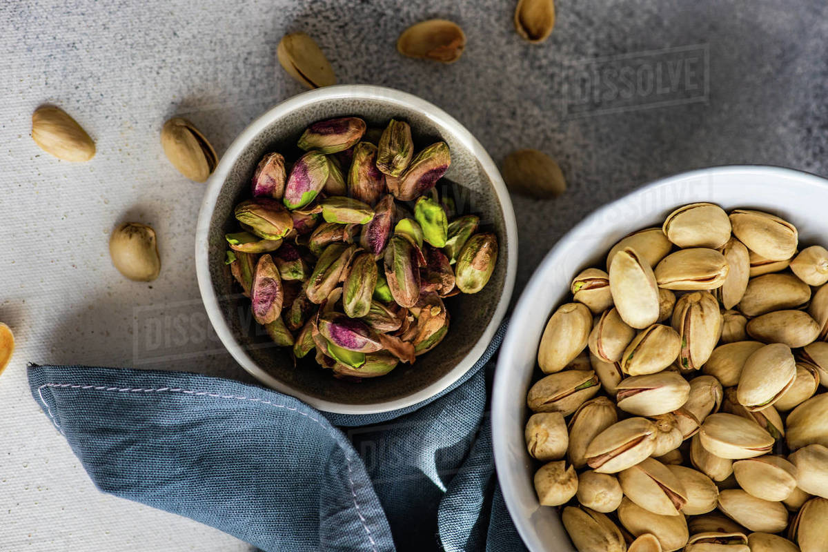 Overhead view of a bowl of pistachio nuts in shells next to a bowl of ...