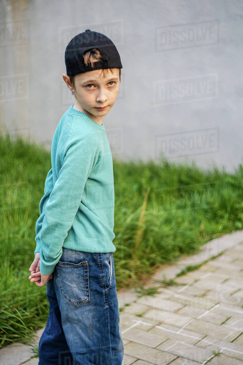 Portrait of a boy standing on a footpath with his hands clasped behind ...