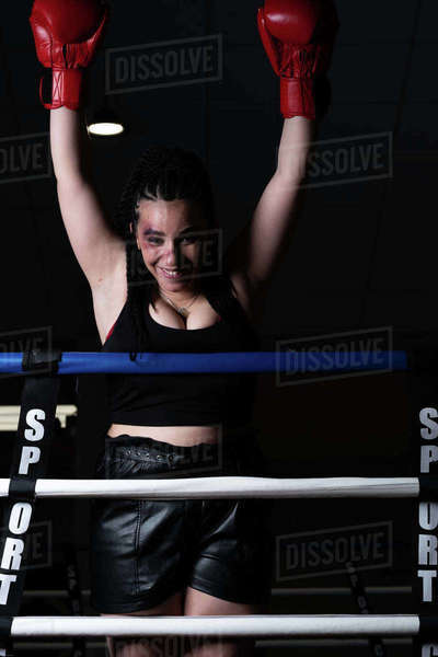Smiling victorious female boxer in a boxing ring with her arms raised ...