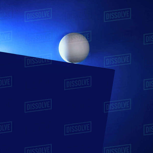 Close-up of a white sphere rolling down the inclined surface of a cube ...