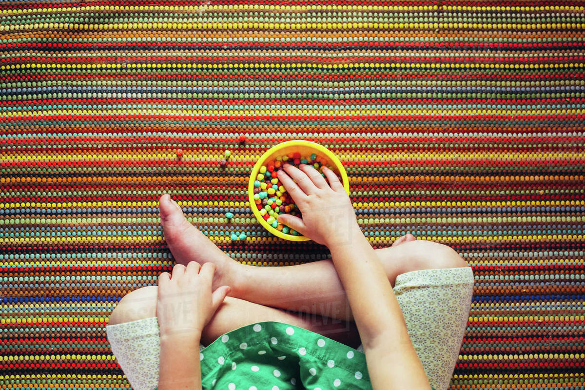 Girl sitting cross legged eating multi-colored snacks - Royalty-free ...