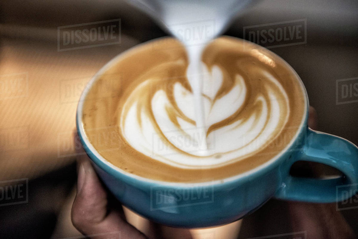Close-up of a person pouring microfoam on a cup of coffee to make a ...