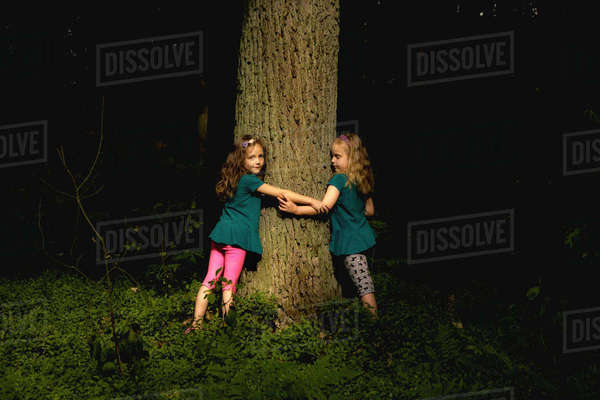 Two girls standing in a garden at night hugging a tree, Poland ...