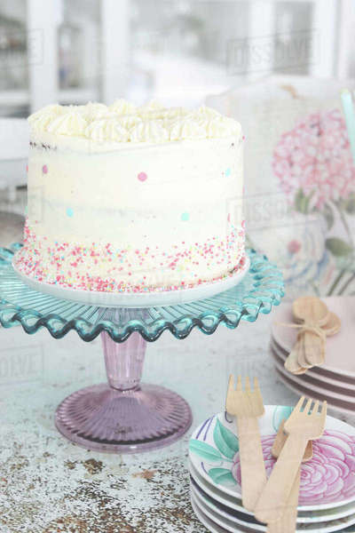 Layer cake with buttercream frosting and sprinkles on a cakestand next ...