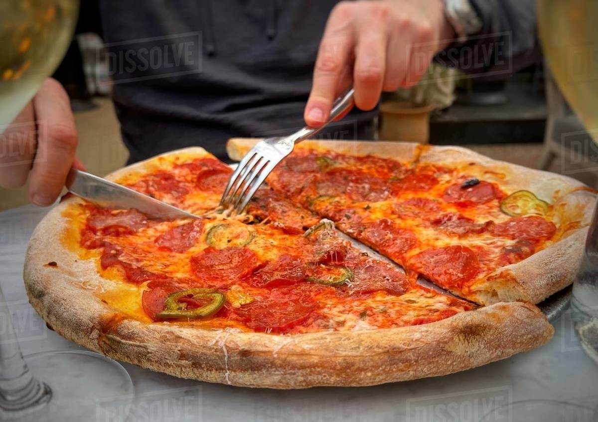 Man eating a pepperoni and jalapeno pizza with a glass of white wine ...