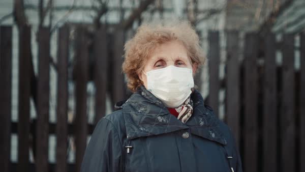 Elderly woman in a respirator protection mask is walking the street ...