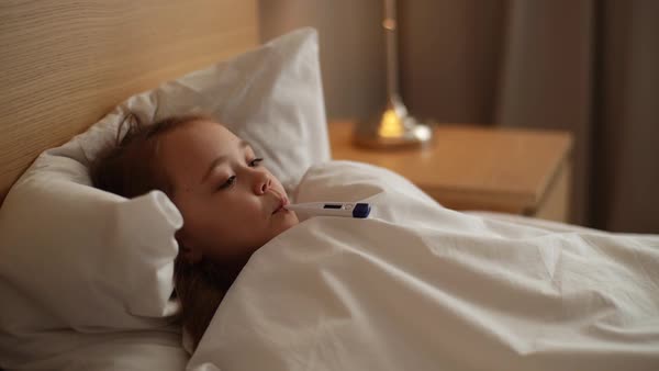 Close-up face of sick girl lying in bed measuring temperature with ...