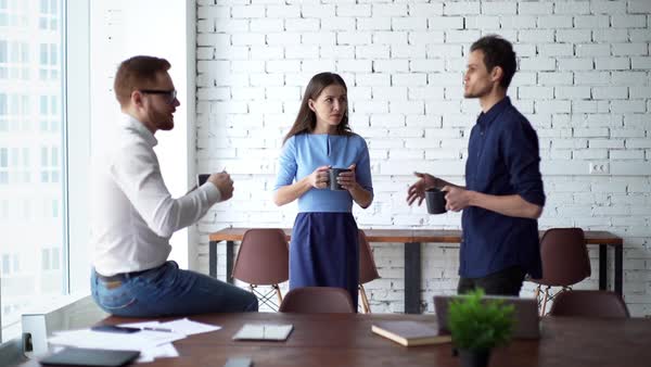 Three friendly coworkers standing in office, drinking coffee and ...