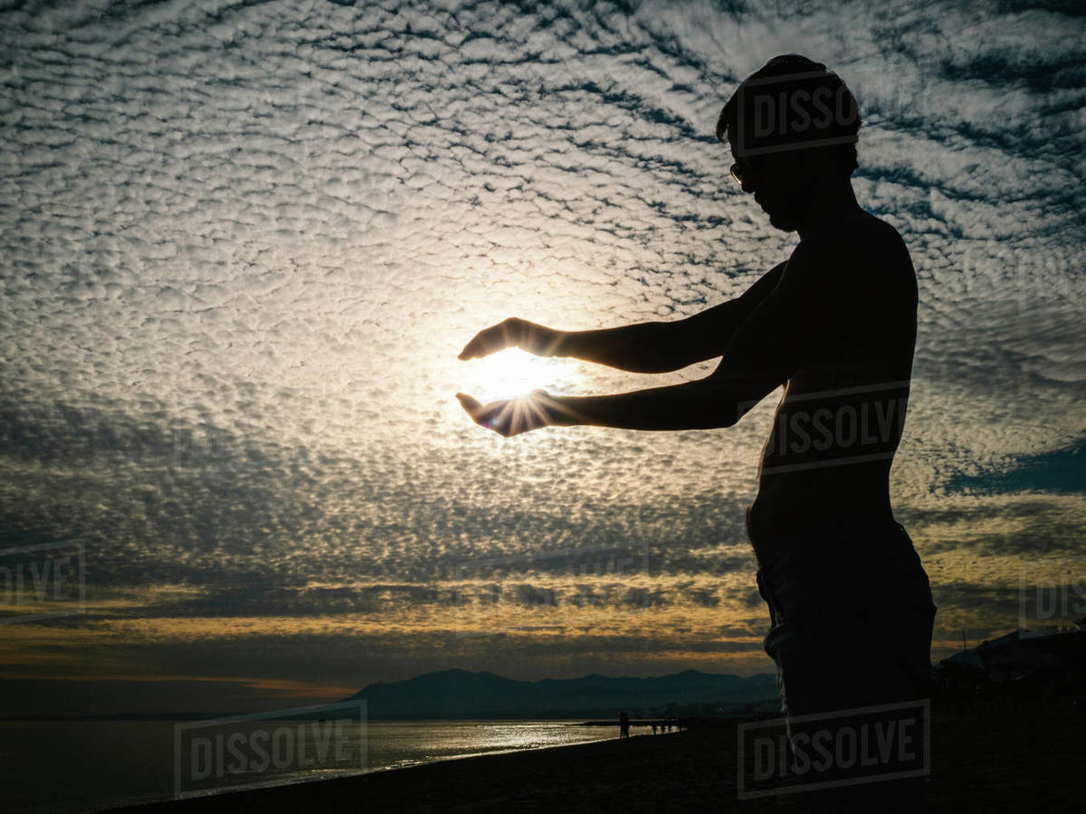 Silhouette of man making gesture of holding sun on background of ...