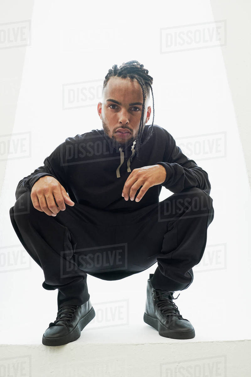 African American man in black clothes with braided hair crouching ...