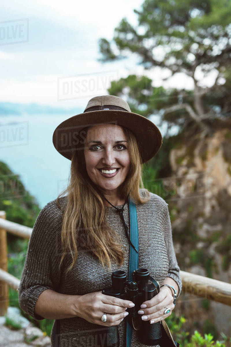 Adult woman observing view with binocular while standing at fence on ...
