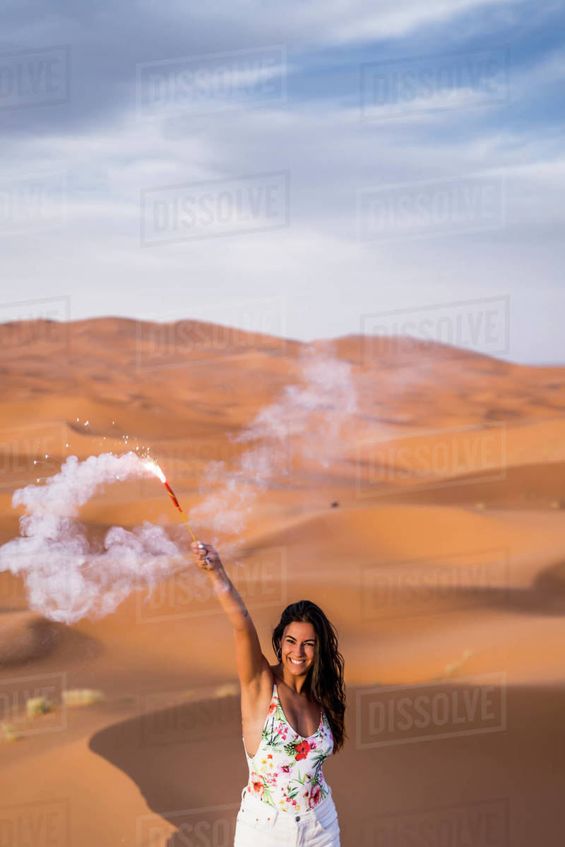 Cheerful stylish brunette holding arm raised with burning smoky ...