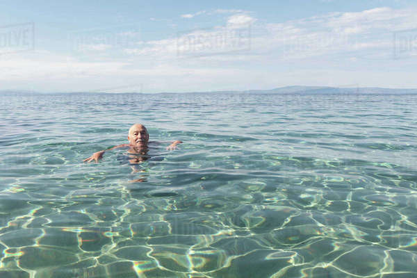 Elderly retired man floating in crystal water enjoying tropical weather ...
