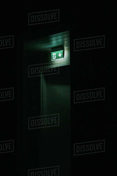 Green exit sign shining over closed door in dark room - Royalty-free ...
