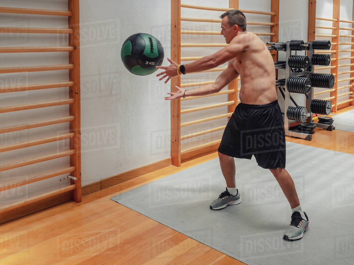 Powerful shirtless male throwing heavy ball against wall during fitness ...