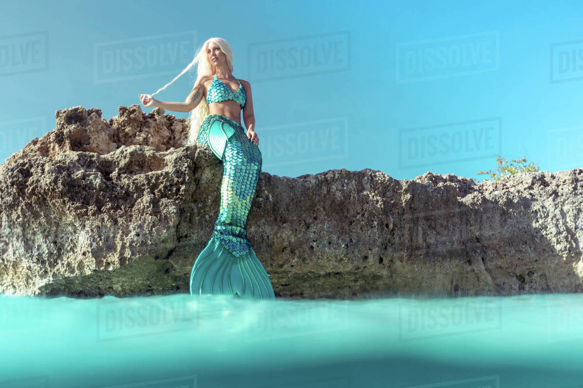 Beautiful young mermaid with blue fishtail relaxing on cliff on sunny ...