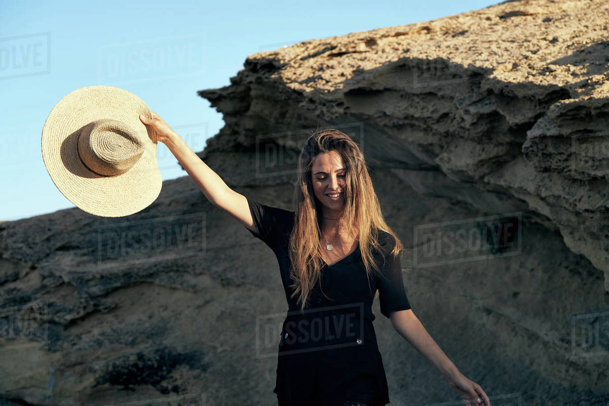 Young long haired smiling female model looking down holding hat in air ...